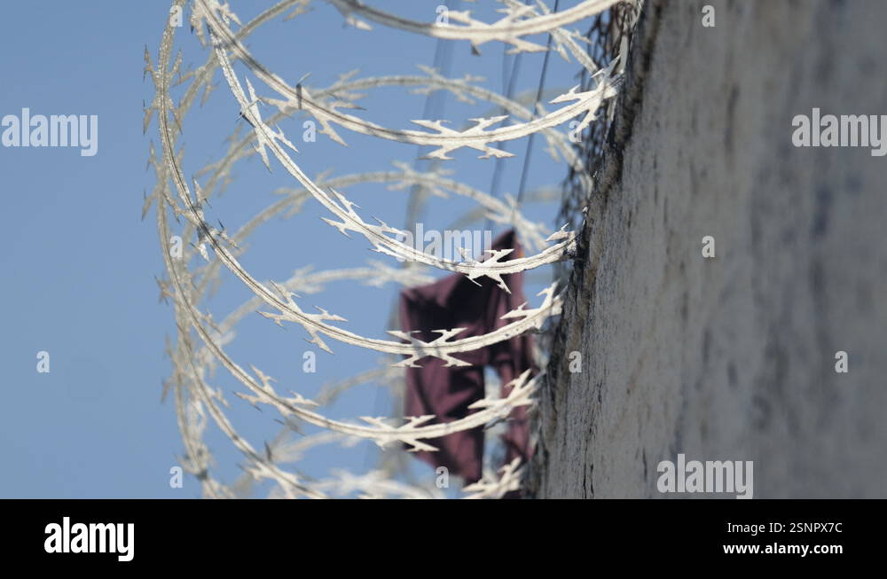 Piece of clothing dangling from razor sharp barbed wire on top of wall ...
