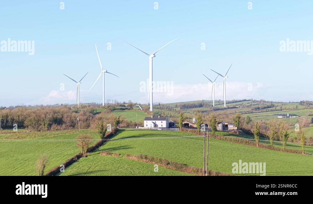 Wind turbines spinning on lush green Irish farmland under a clear blue ...
