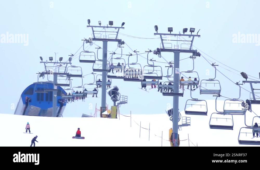 Skiers glide down a snow-covered hill as a chairlift rises against the ...