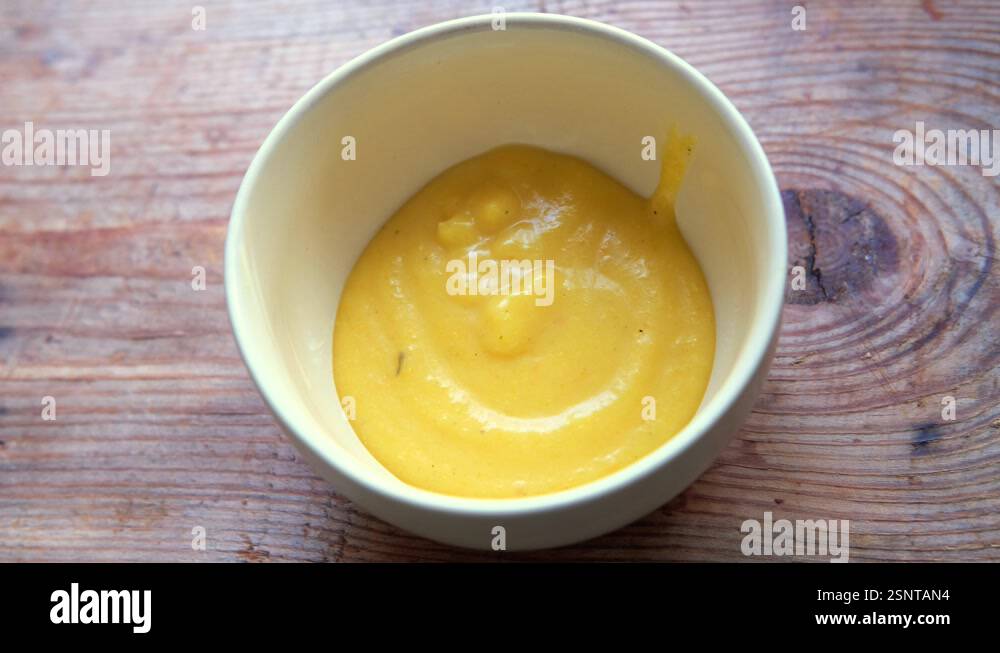 pouring yellow pumpkin puree soup with ladle into bowl,on wooden ...