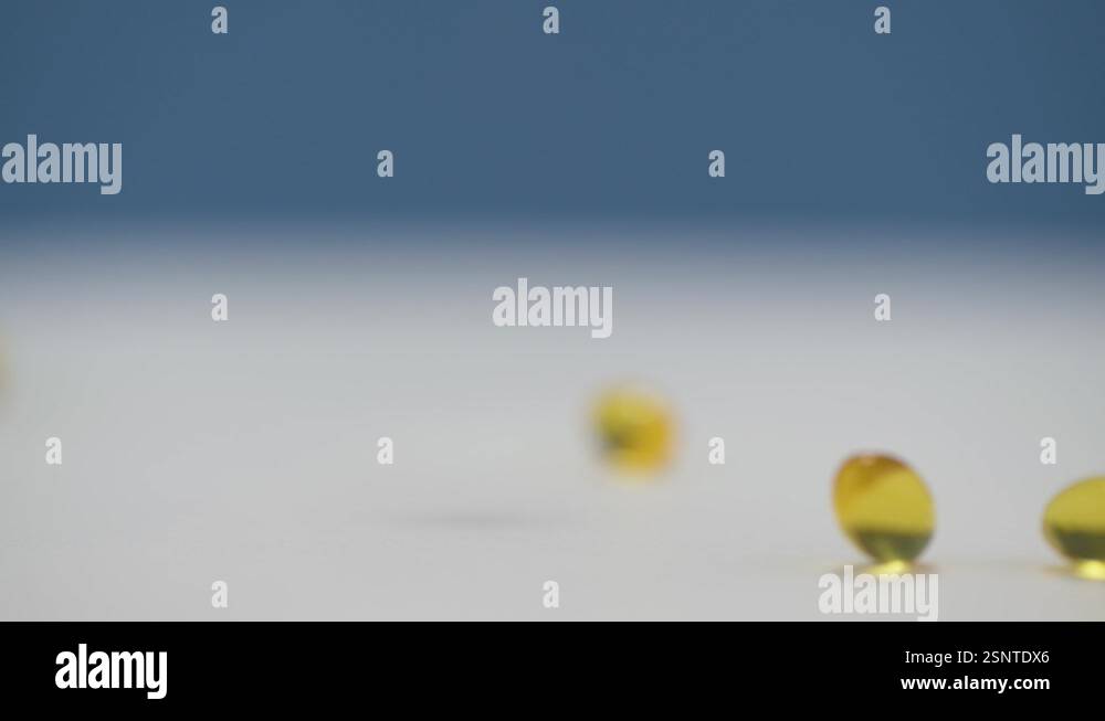 Slow motion 4K of yellow omega-3 capsules dropping onto white surface ...