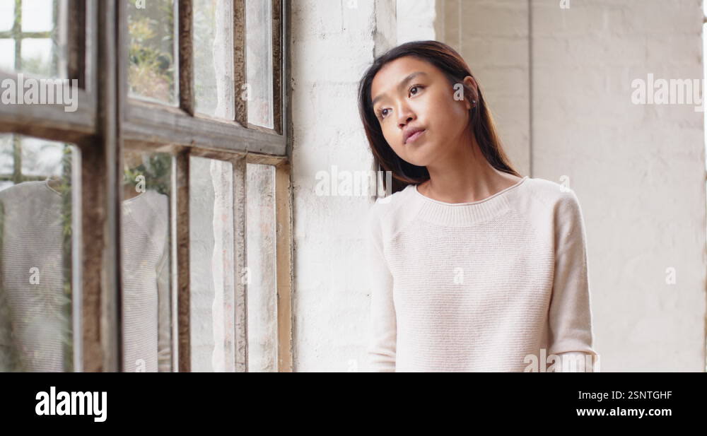 Gazing out window, asian young woman reflecting quietly in living room ...