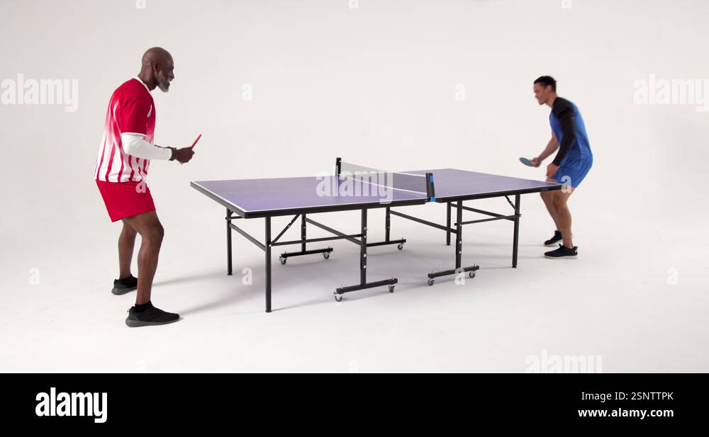 Playing table tennis, two men competing intensely in studio setting ...
