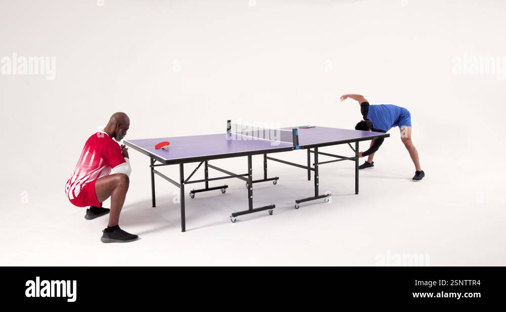 Playing table tennis, two men competing intensely in studio setting ...