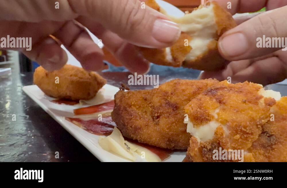Close-up view of the hands of a white man eating spanish ham croquettes ...