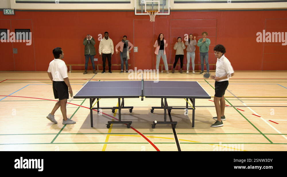 Playing table tennis, two men competing in school gymnasium with ...