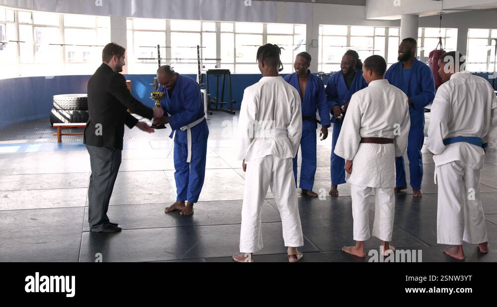 Celebrating victory, judo team in blue uniforms holding trophy in dojo ...