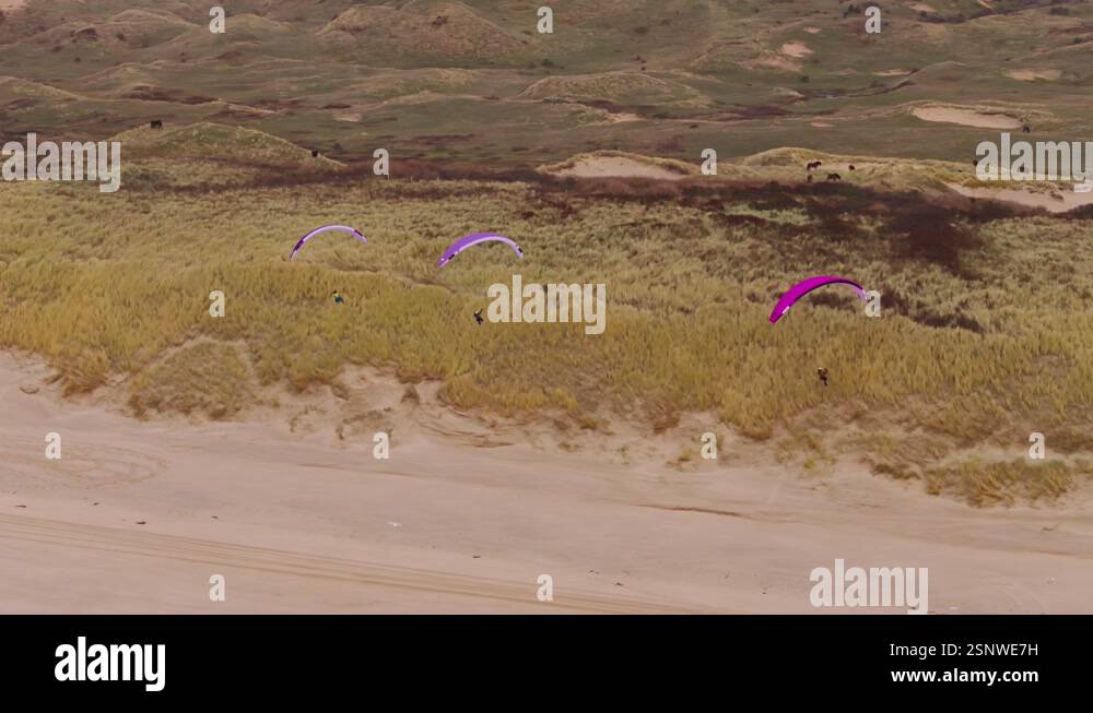 Paragliders fly by sand dunes in Castricum, Netherlands, wide drone ...