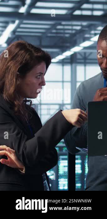 Vertical video Developers in data center workspace coding on laptop, analyzing metrics ...