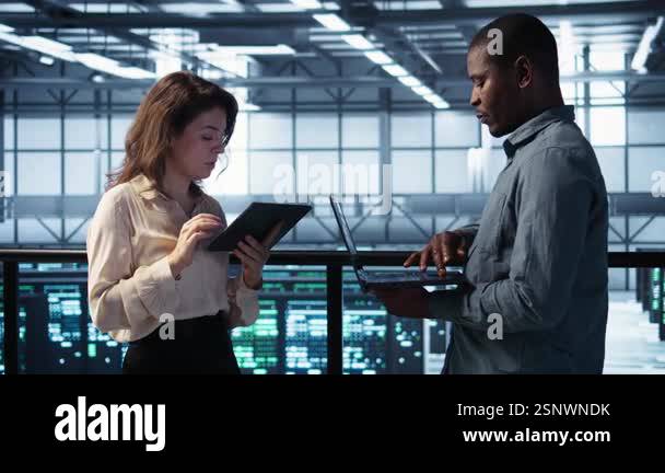 Smiling admins using laptop in data center, managing server virtualization. Cheerful IT ...