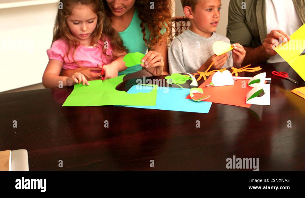 Parents and children making paper shapes together at the table Stock ...