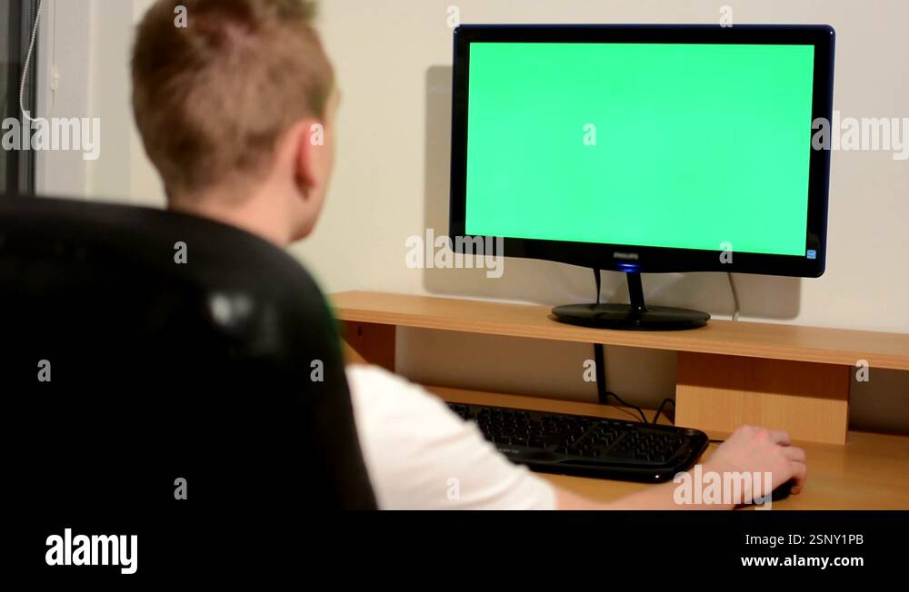 Young man writes on the keyboard and looks at the monitor - green ...