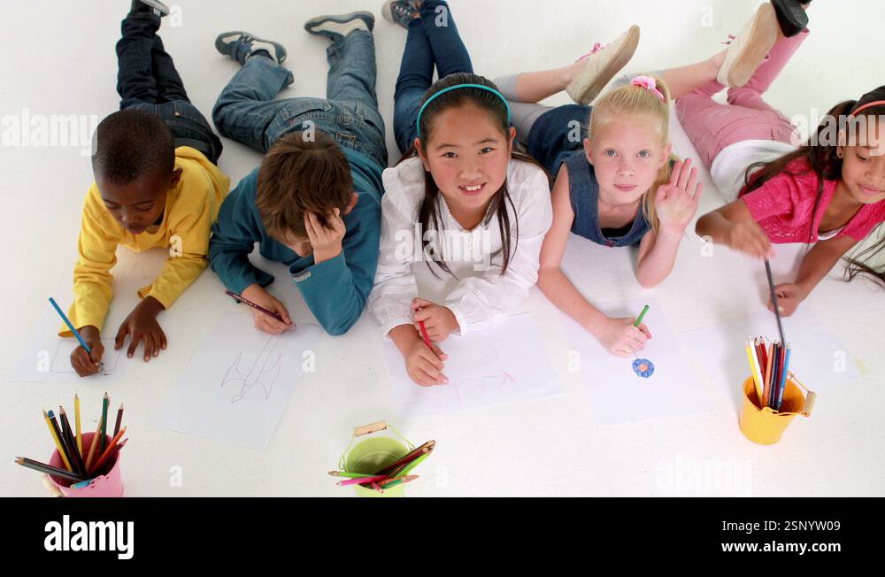 Cute children lying on floor drawing on paper and waving at camera ...