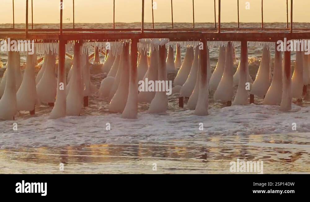 Big ocean waves smashing the frozen pier in ice at sunrise. Slow motion ...