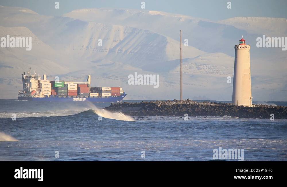 Fully loaded cargo ship sails by snowy mountains, Grotta lighthouse ...