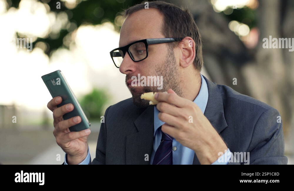 Young businessman with smartphone, eating slice of bread in cafe in ...