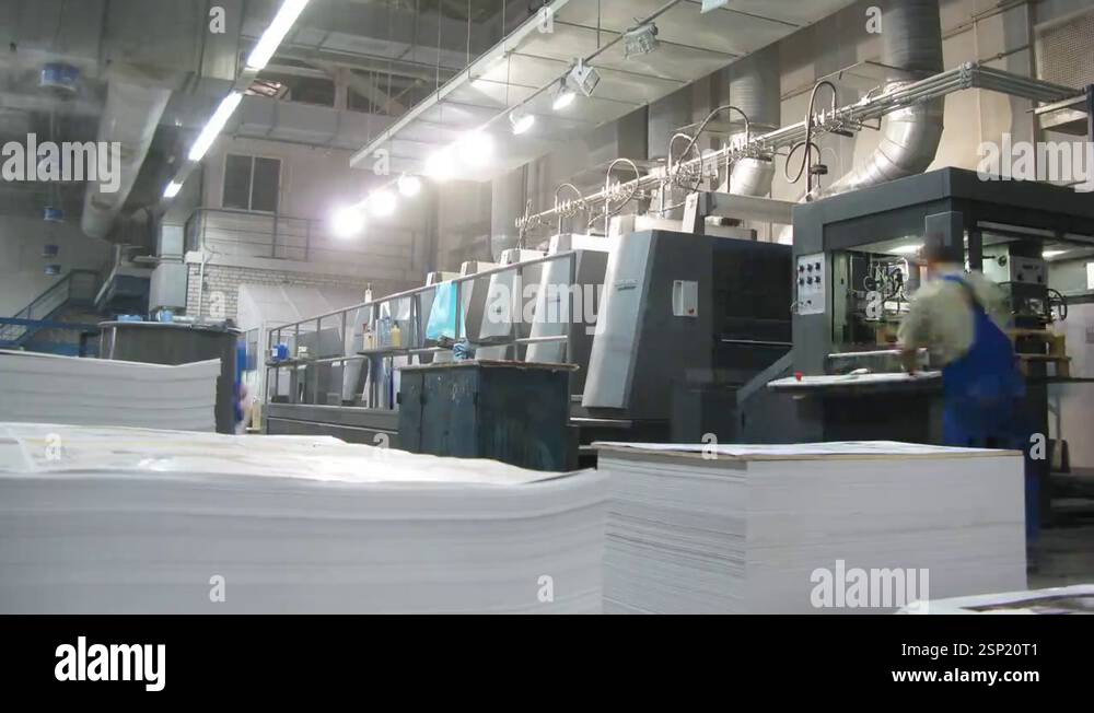Workers work in printing machines, in foreground a pile of paper Stock ...