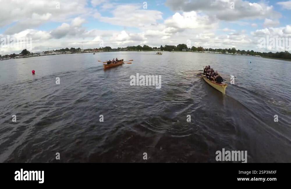 Aerial of two crew rowing boats following athletes racing for first ...
