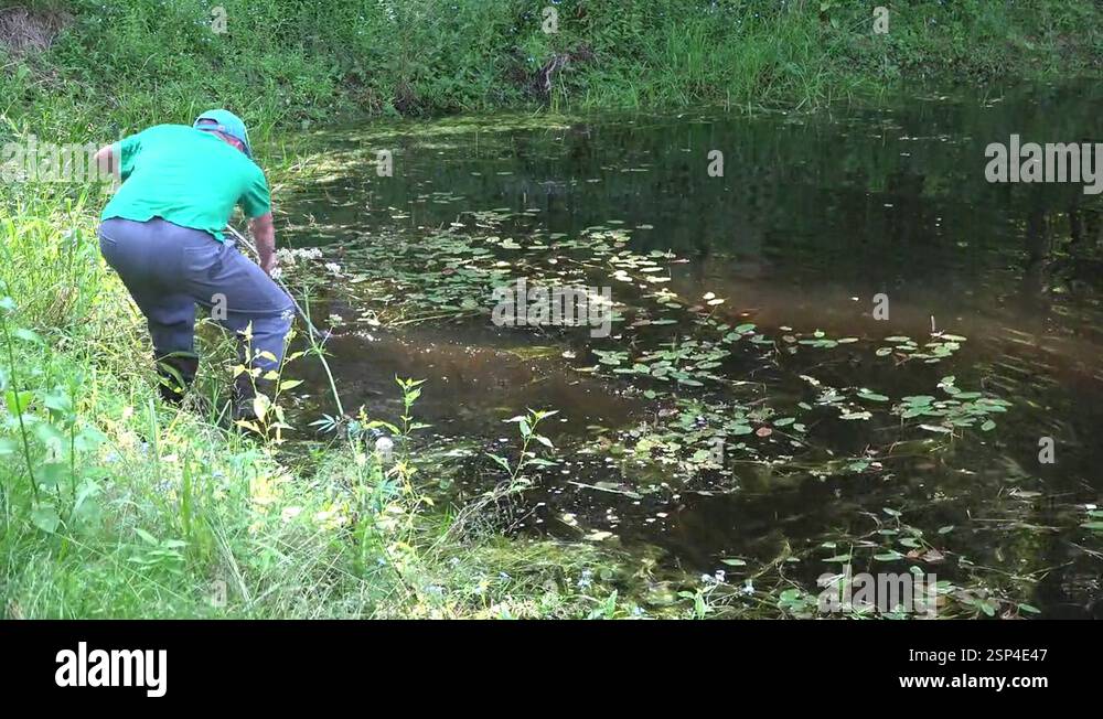 fish breeding farm worker with scythe tool clean pond from grass. 4K ...