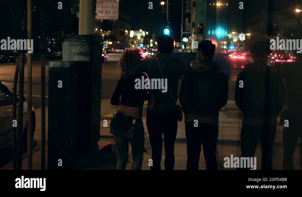 Group of friends walk down a city sidewalk at night with arms around ...