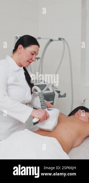 Cosmetologist doctor makes a woman cavitation LPG vacuum roller massage procedure on back ...
