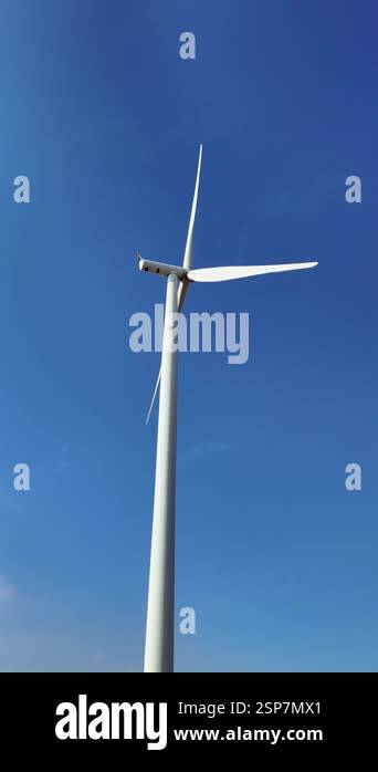 A towering wind turbine against a clear blue sky represents renewable energy and sustainability ...