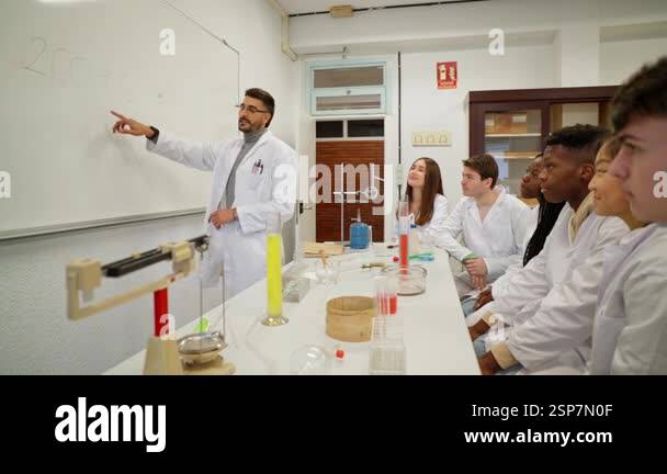 Chemistry instructor demonstrating scientific principles, wearing lab coat and explaining ...
