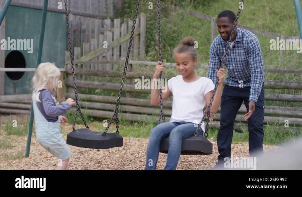 4K Family playing on swings in playground, parents pushing little girls ...