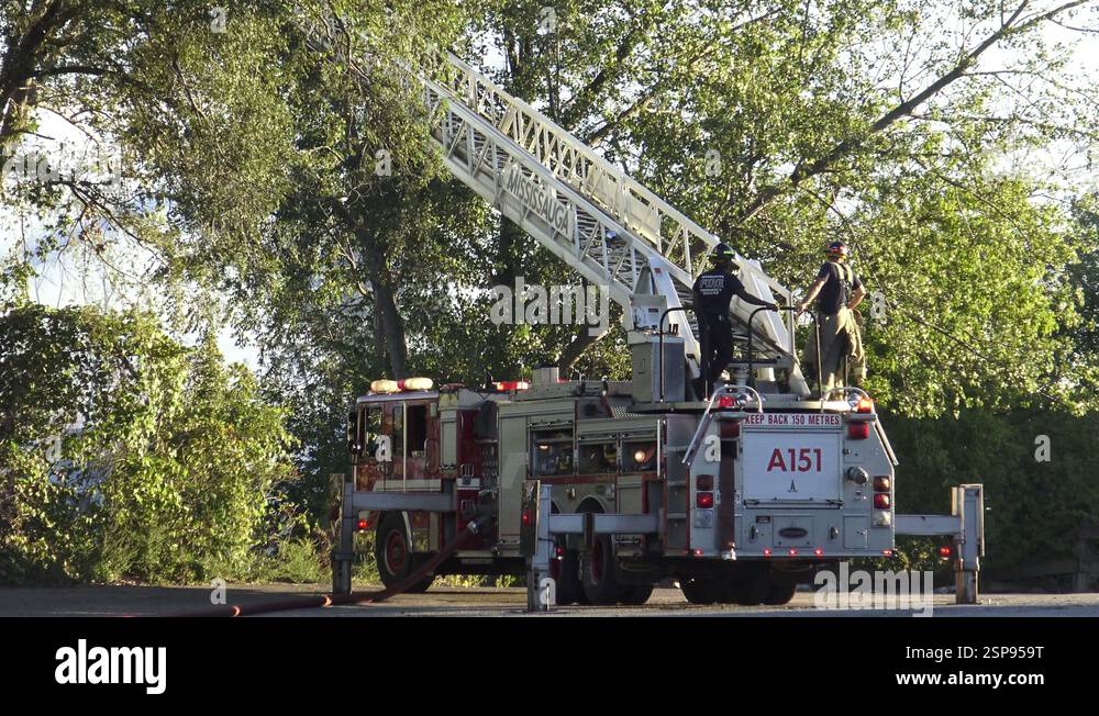 Two firemen on top of a fire truck with fire hose attached to a ladder ...