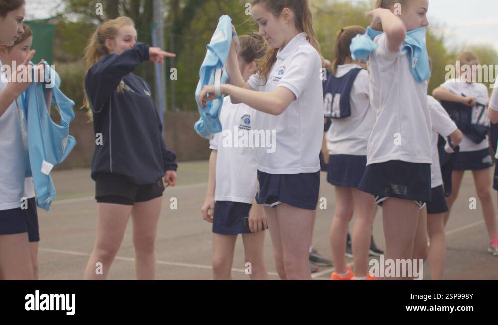 4K 2 Young netball teams on outdoor court putting on bibs at beginning ...