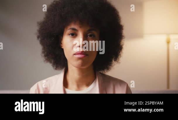 Smiling woman with Afro-hairstyle rests in living room. Young Latin ...