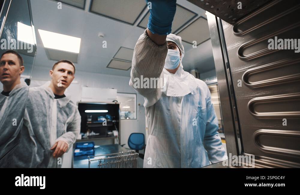 Scientist in hazard sterile suit pull metal sheet out laboratory oven ...