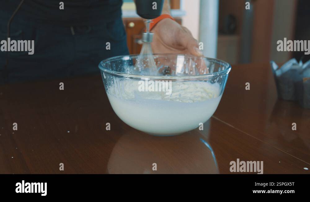 Buffed man making whiped creme in glass bowl using whisk at kitchen ...