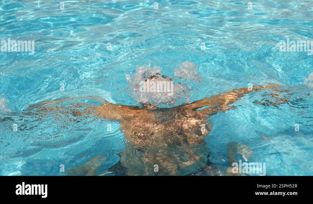 A man dives into the pool with blue water. Splashes fly in different ...
