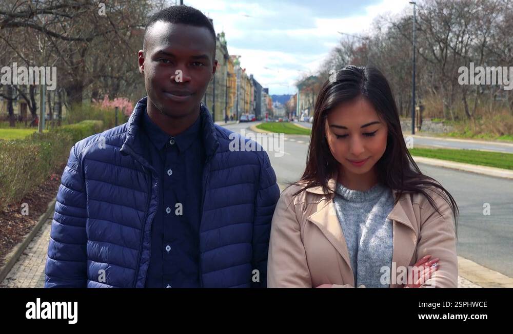 A young black man and a young Asian woman nod at the camera in a street ...