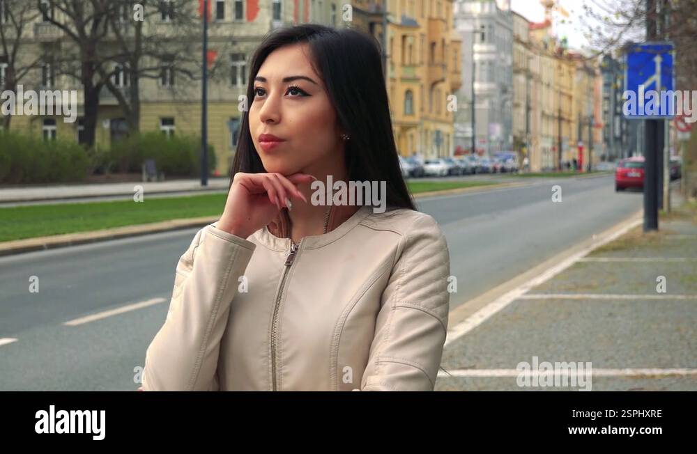 A young Asian woman broods while walking back and forth in a street in ...