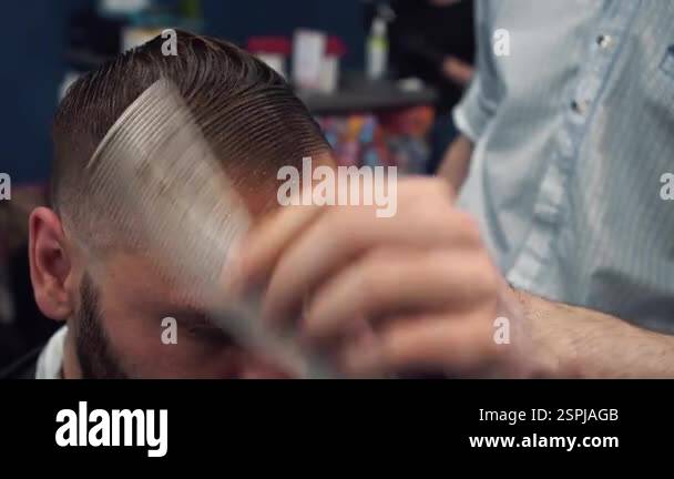 In a barbershop, a professional barber expertly combs a clients wet ...