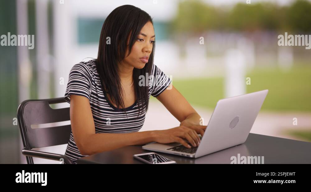 Cute black female typing on laptop outdoors pauses to check messages on ...
