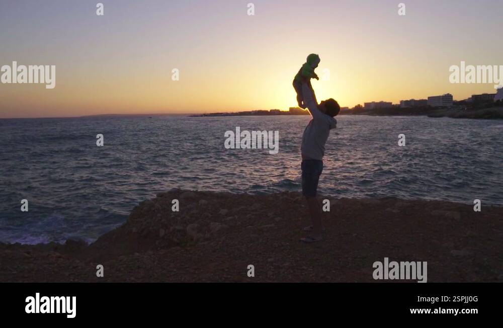 Father holds his baby boy over the head. Silhouettes against sea sunset ...