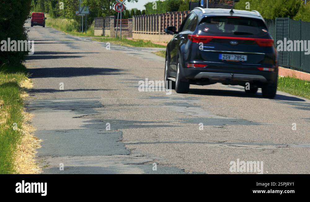Road in poor condition with passing cars next to the fences of houses ...