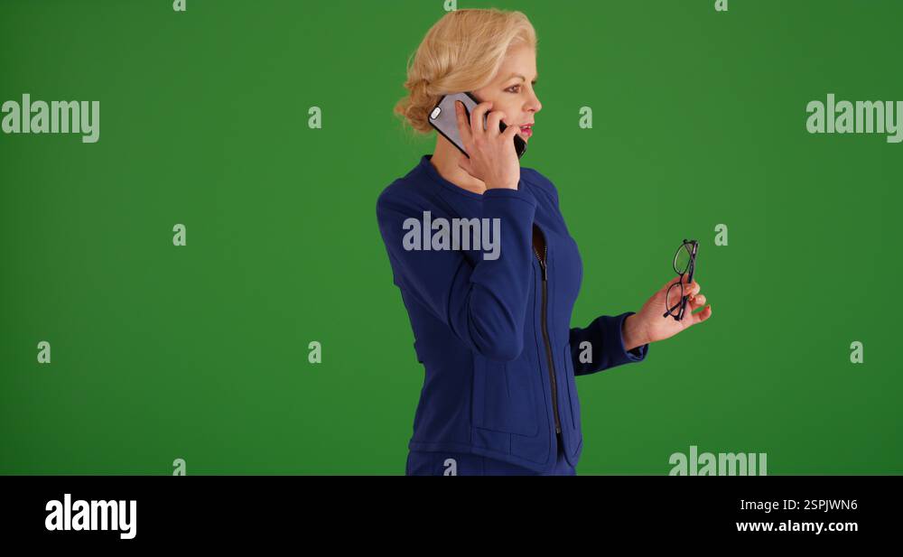 Portrait of female CEO holding glasses talking on cellphone on green ...