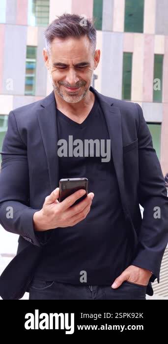 A confident businessman in a black suit holds out his smartphone with a ...