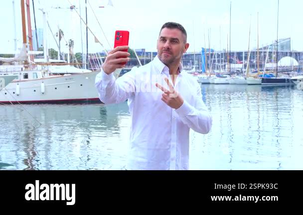 Smiling man in a white shirt taking a selfie with a red smartphone near ...