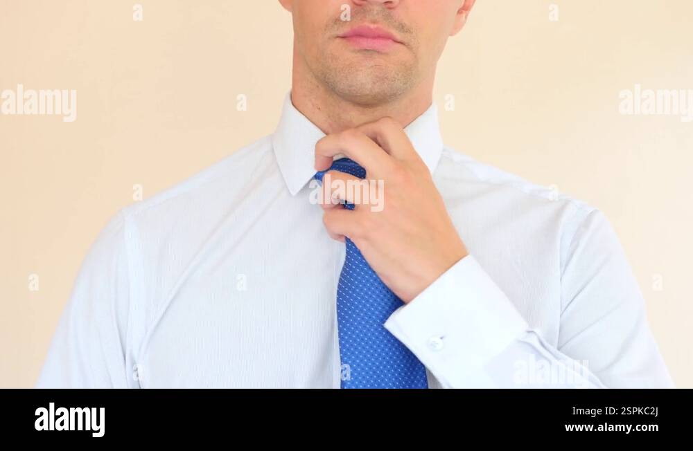 A business man takes off his blue tie and unbuttoned the top button on ...