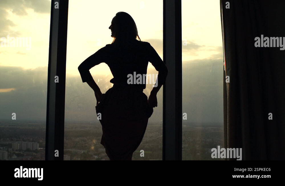 Silhouette of happy woman dancing by window at home during sunset ...