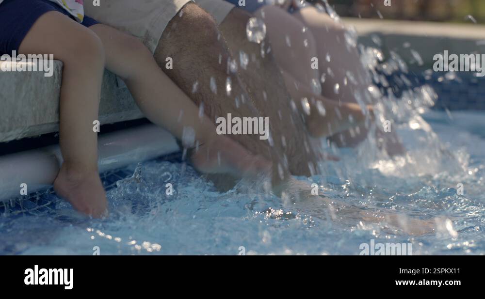 Detail of family's legs at side of swimming pool splashing feet in ...