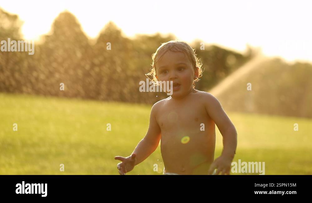 Infant toddler baby boy running in slow-motion120fps at water sprinkles in green Stock Video ...