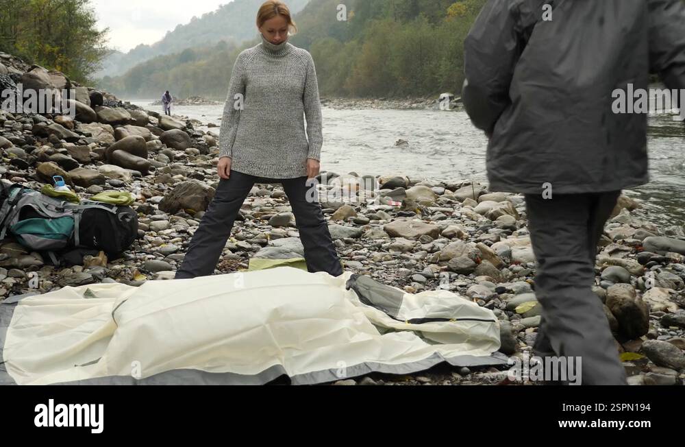 4k. a guy and a girl puts a tourist tent on the shore of a mountain ...