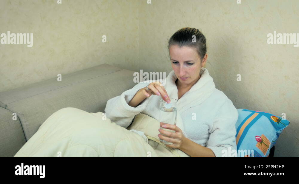 Sick young girl in a home dressing drinks an effervescent tablet of ...