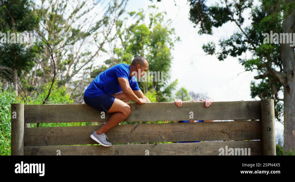 Male trainer assisting fit woman to climb over wooden wall during ...